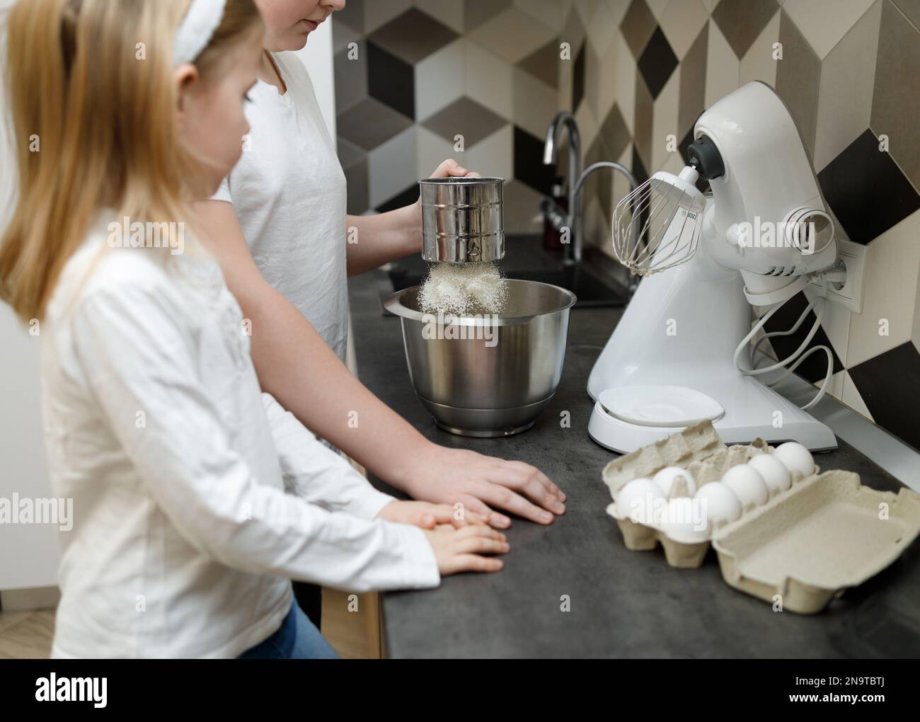 Sister in bunny ears looking at brother sifting flour, helping parents ...
