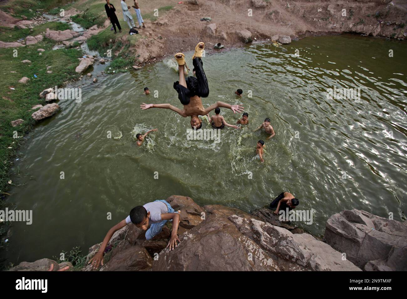 A Pakistani boy jumps from a hill in to a stream, where he and other ...