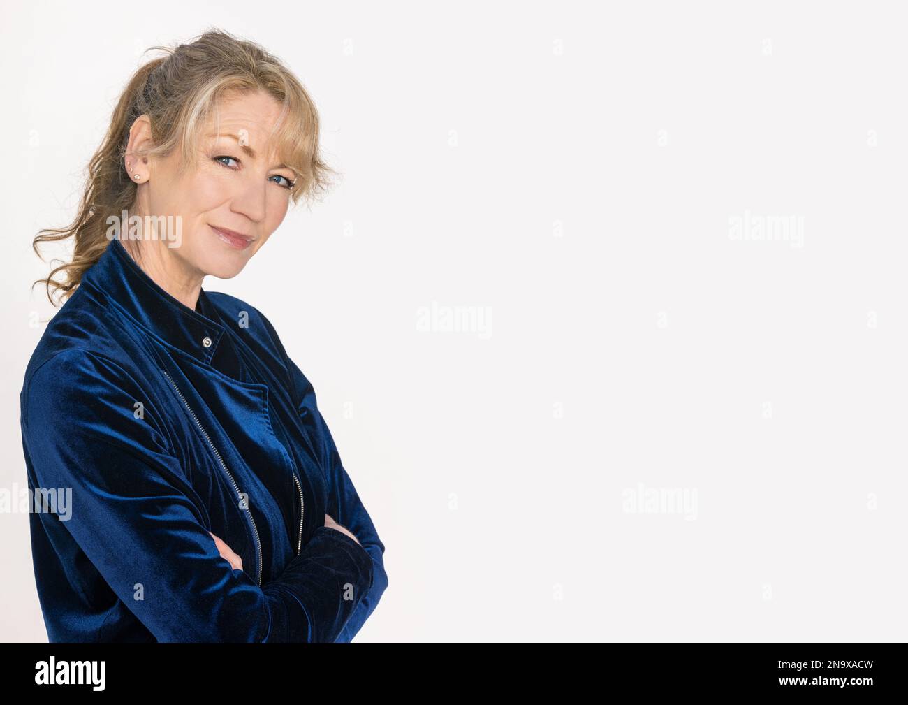 Attractive happy smiling female middle aged woman wearing a blue velvet jacket studio portrait ...