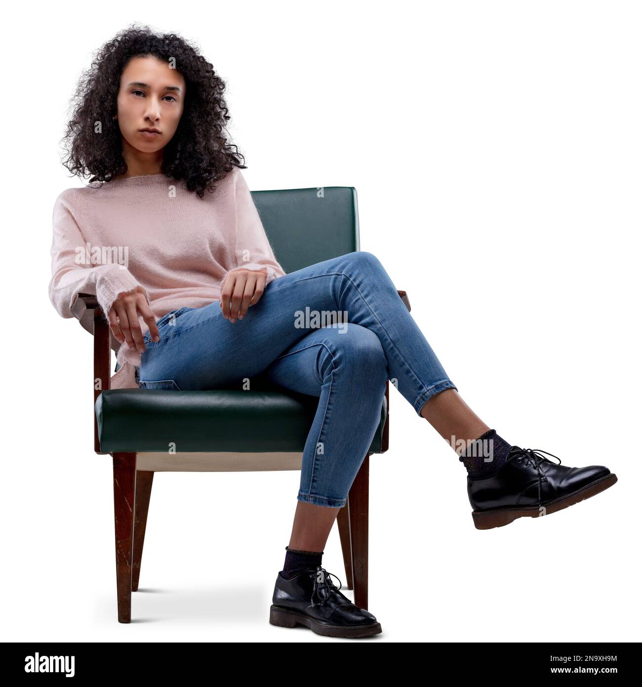 Young curly-haired woman sitting in a chair with her legs crossed and ...
