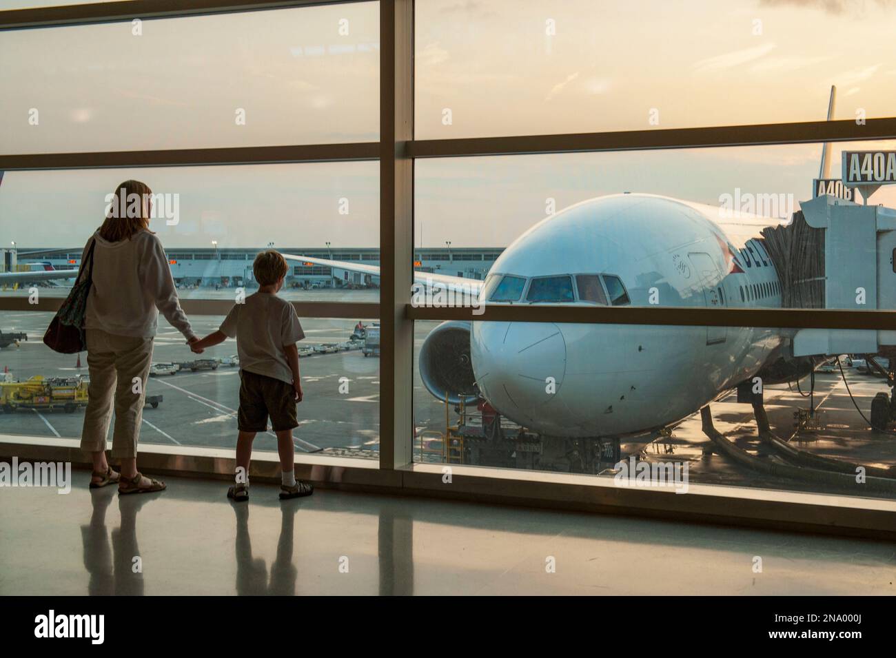Woman and young son stand holding hands and look out airport window at ...