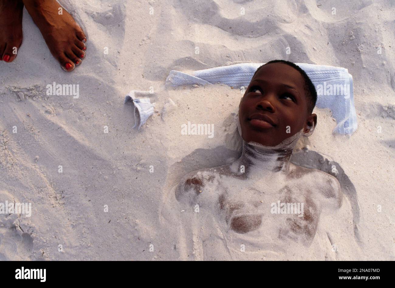 Young boy is buried in the white sand on a beach while on vacation in ...