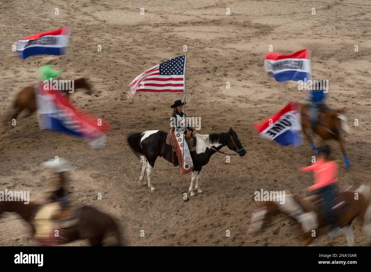 Rodeo queens on horses circle a rodeo queen who is holding the American ...