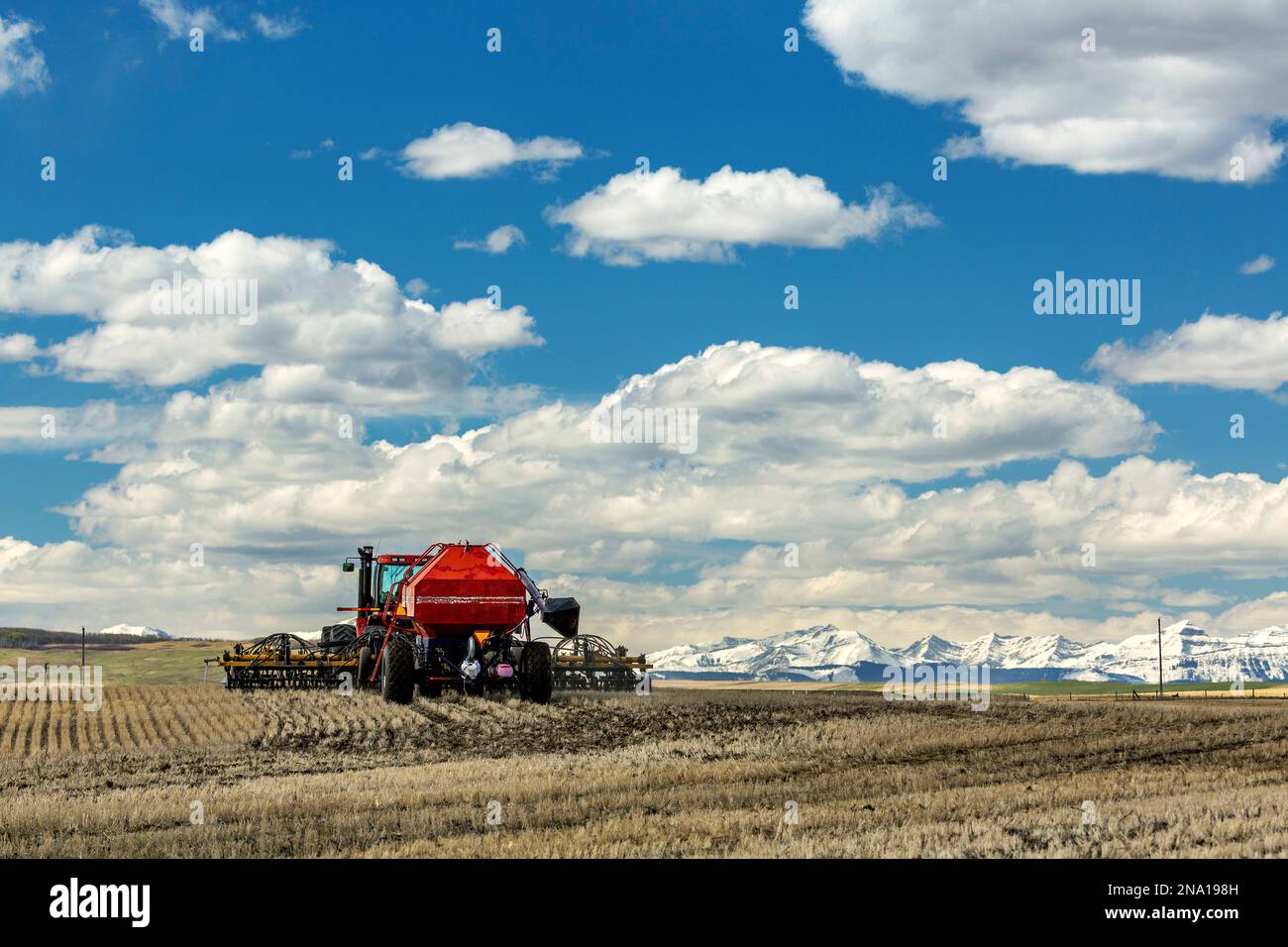 Tractor and seeder, seeding a field with snow covered mountain range in ...
