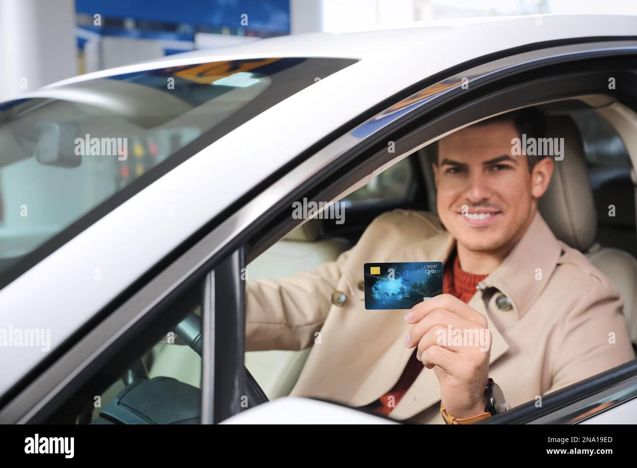 Man sitting in car and showing credit card at gas station, focus on ...