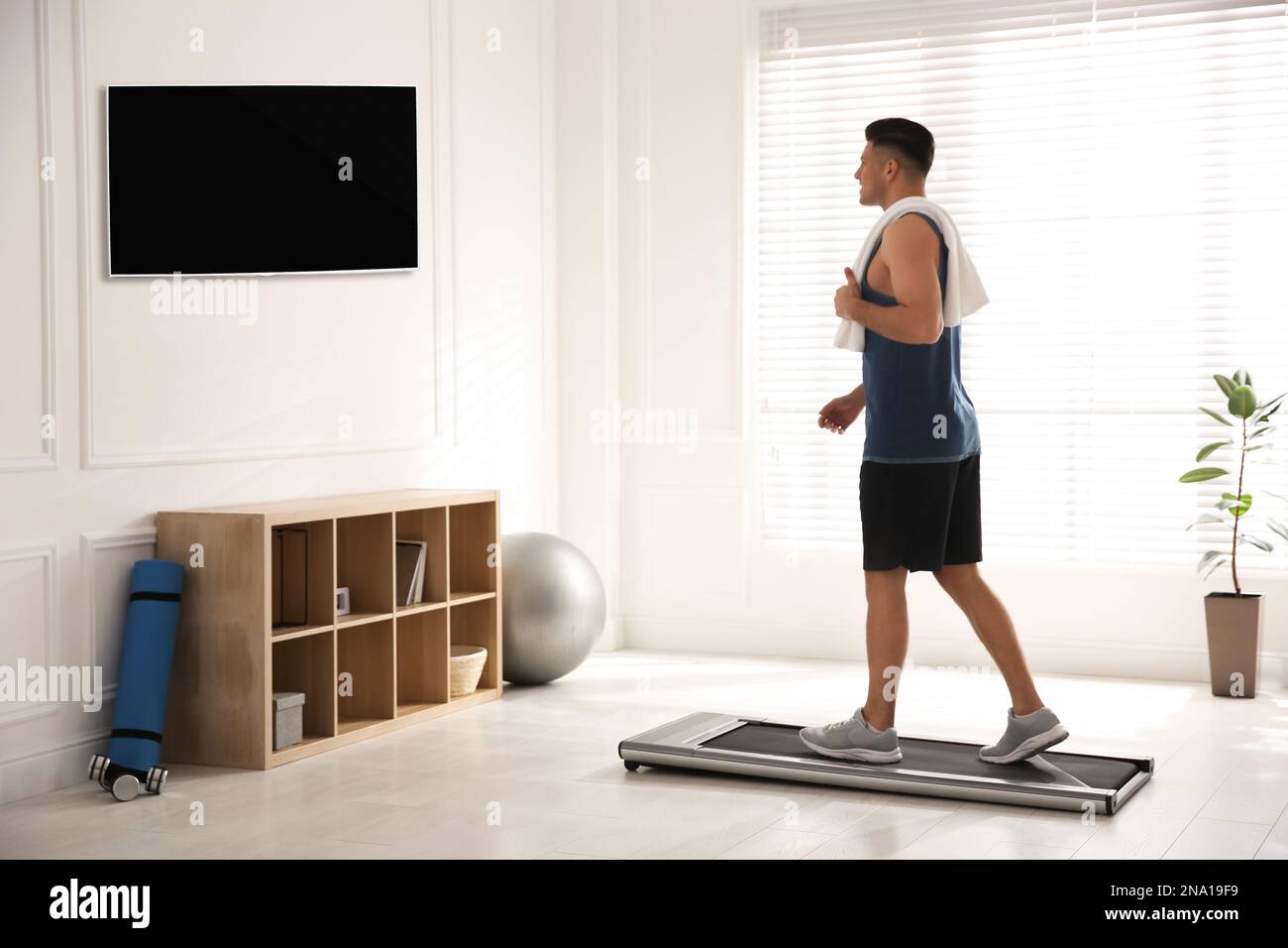 Sporty man training on walking treadmill while watching TV at home ...