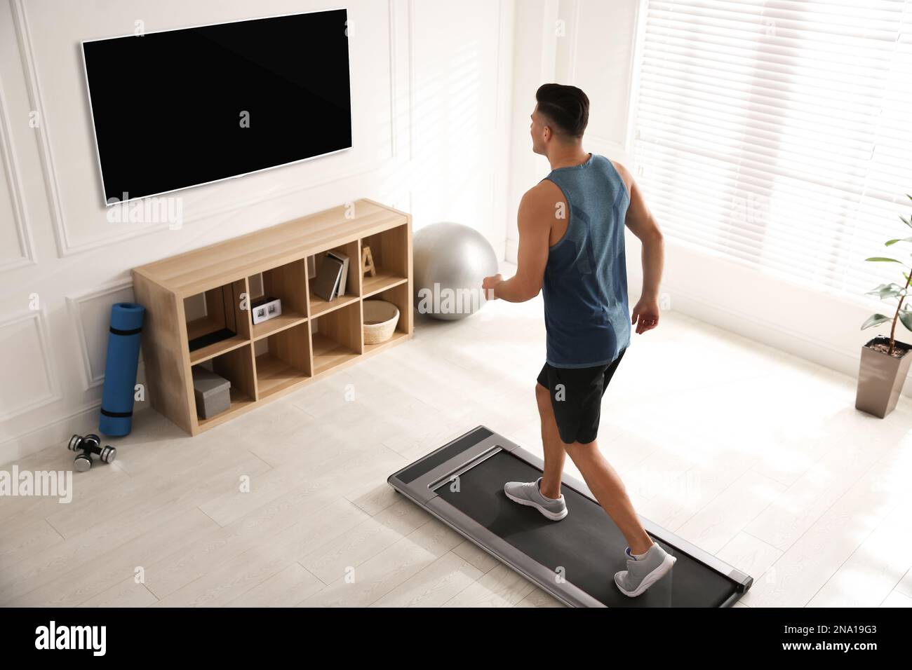 Sporty man training on walking treadmill while watching TV at home ...