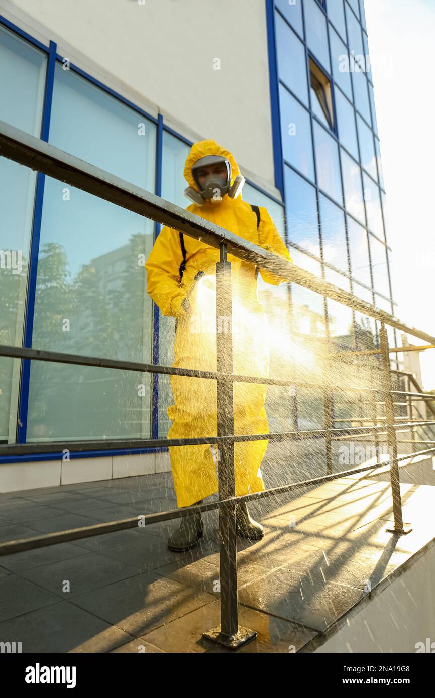 Person in hazmat suit with disinfectant sprayer cleaning metal railing ...