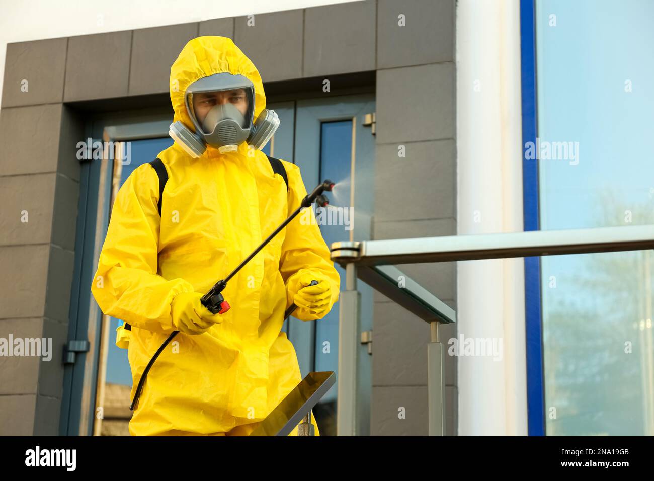 Person in hazmat suit with disinfectant sprayer cleaning metal railing ...