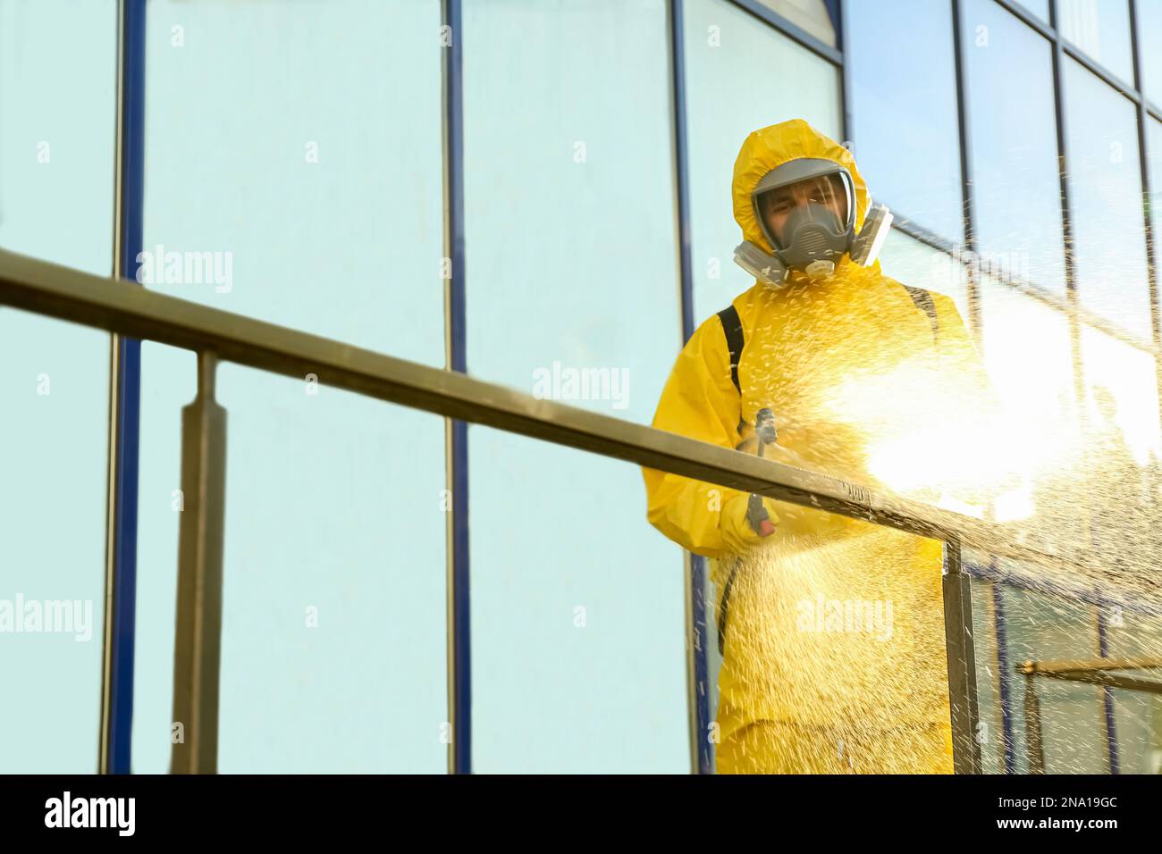 Person in hazmat suit with disinfectant sprayer cleaning metal railing ...