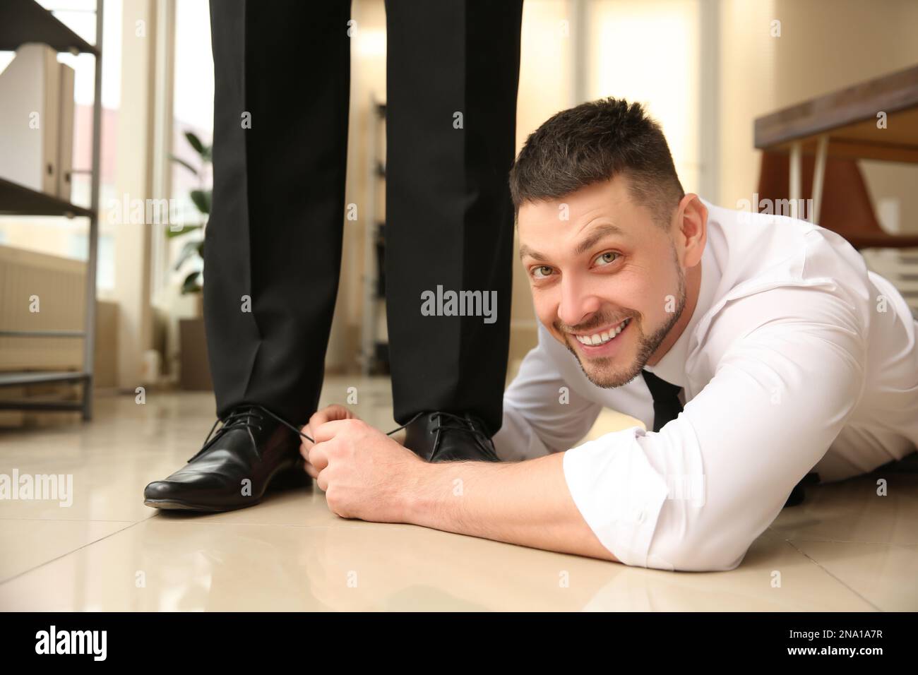 Man tying shoe laces of his colleague together in office, closeup ...