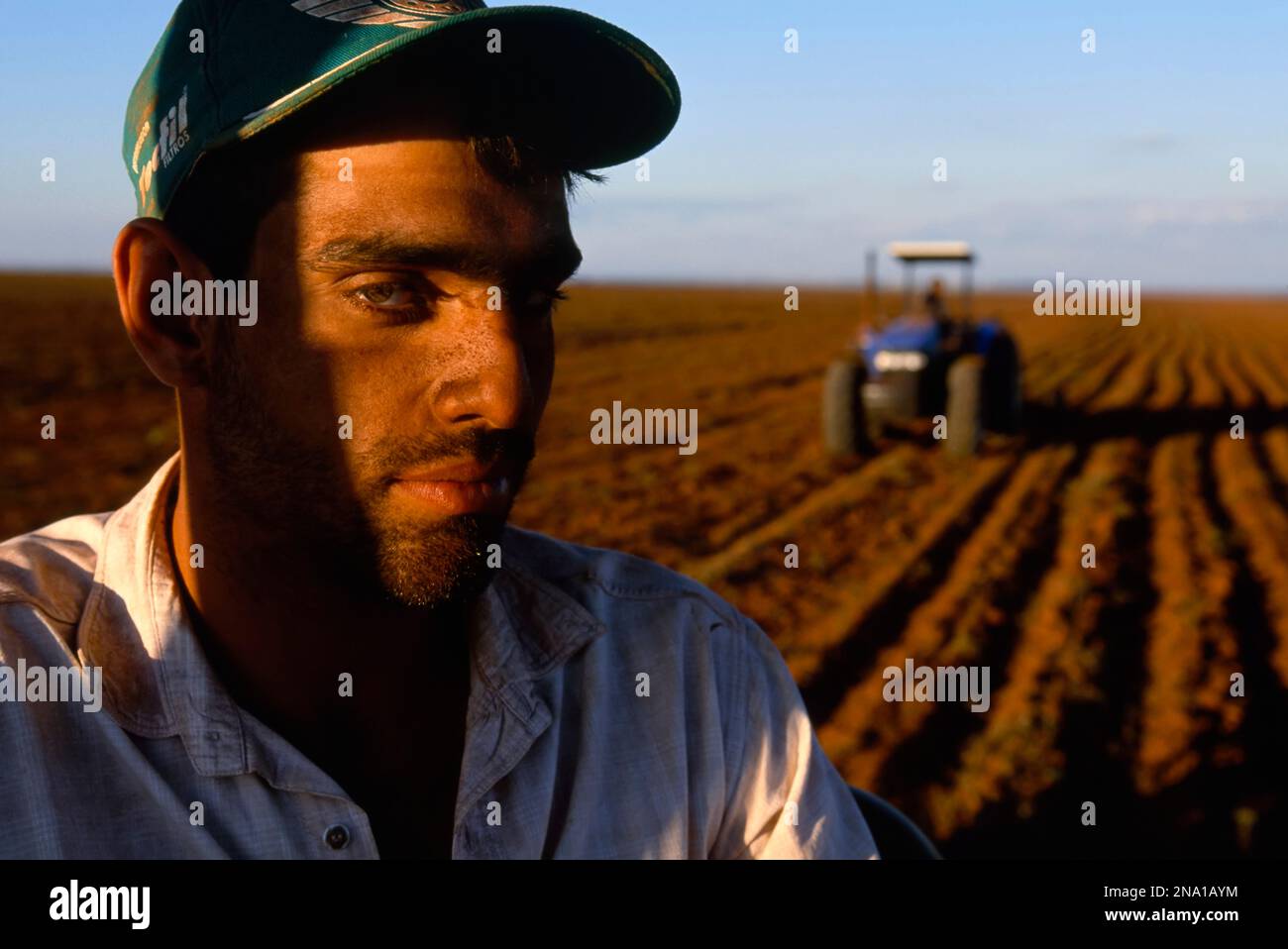 Farmer standing on vast farmland with his tractor in the background ...
