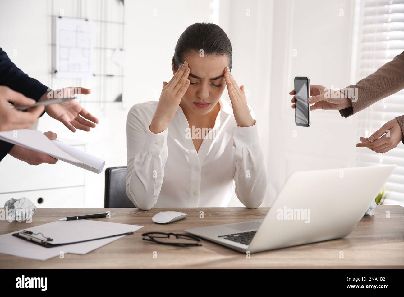 Stressed and tired young woman surrounded by colleagues at workplace ...