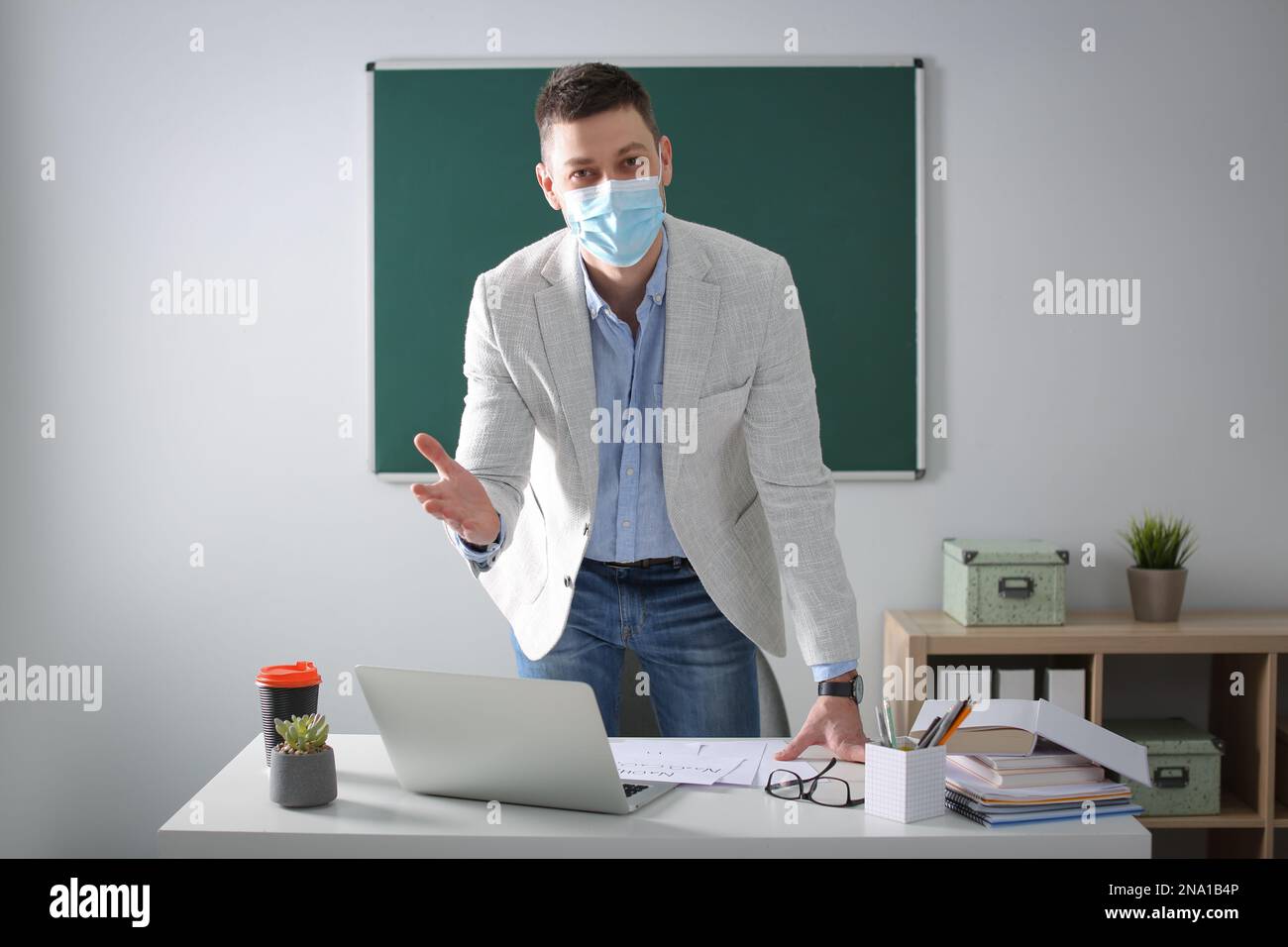 Teacher with protective mask conducting lesson in classroom. Reopening ...