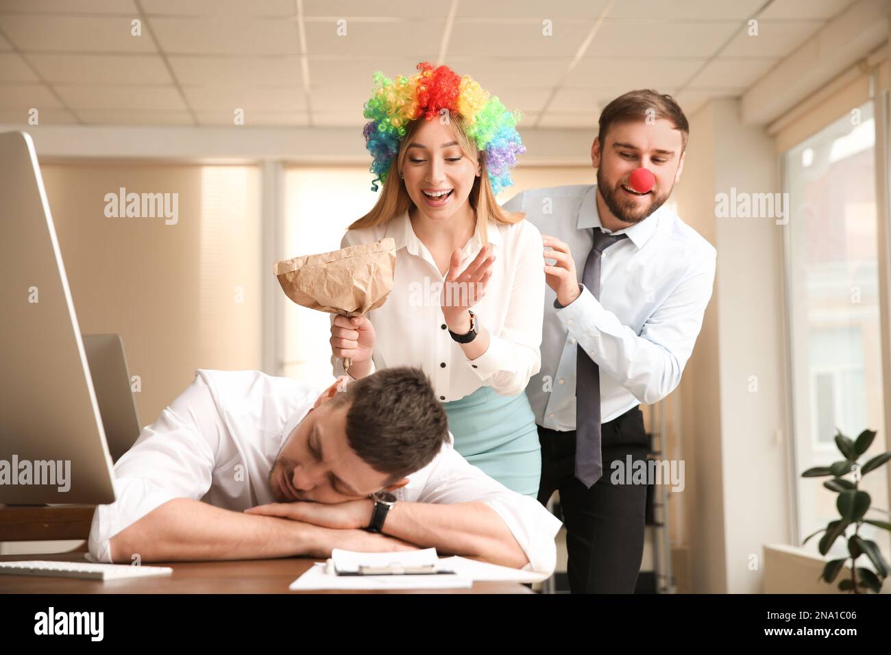 Coworkers popping paper bag behind their sleeping colleague in office ...
