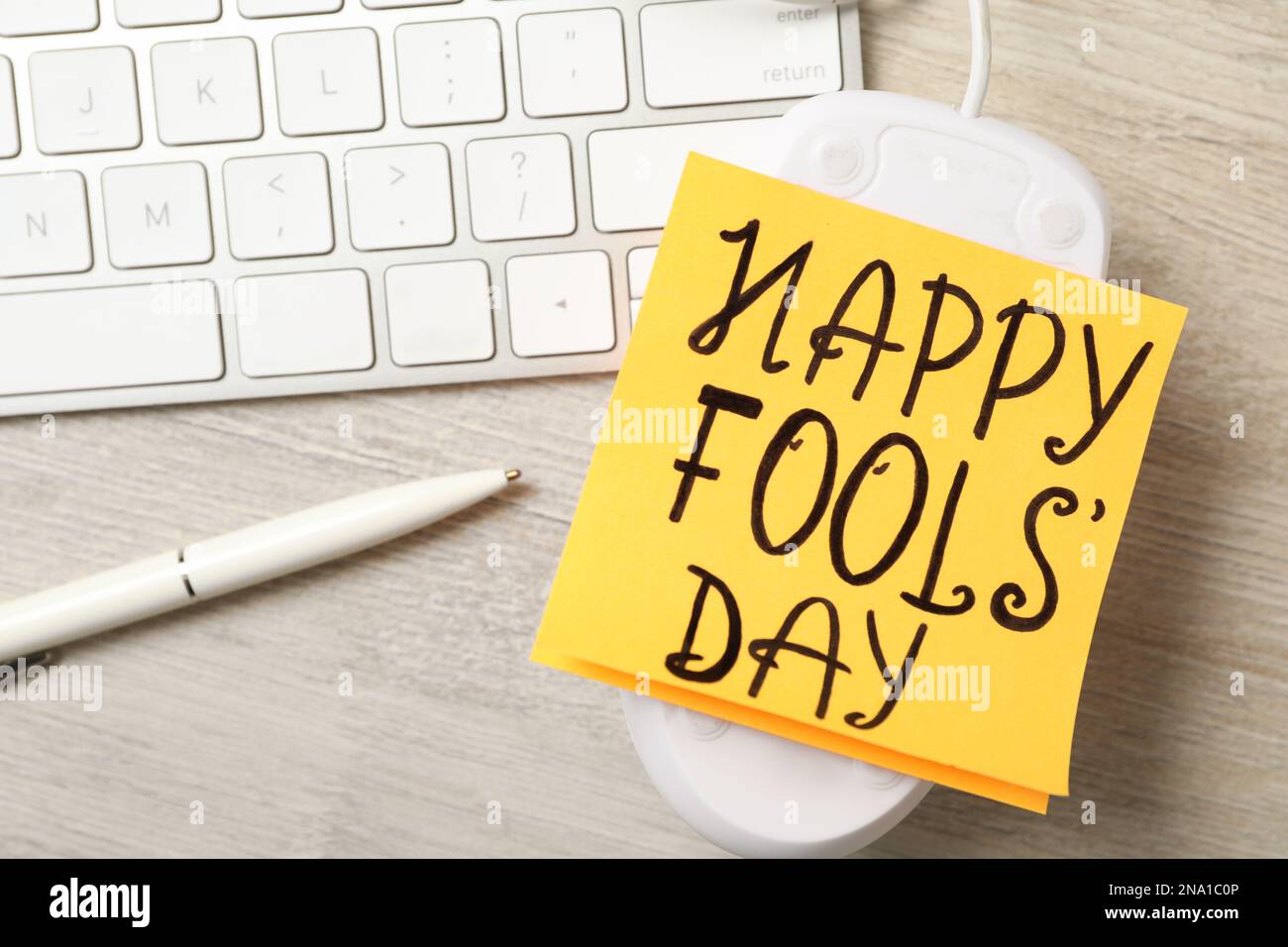 Computer mouse with Happy Fools' Day note near keyboard on wooden table ...