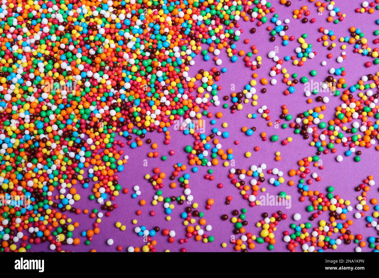 Colorful sprinkles on purple background, flat lay. Confectionery decor ...