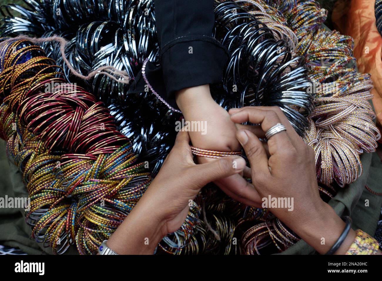 A Pakistani female vendor helps a customer to try on bangles at a ...