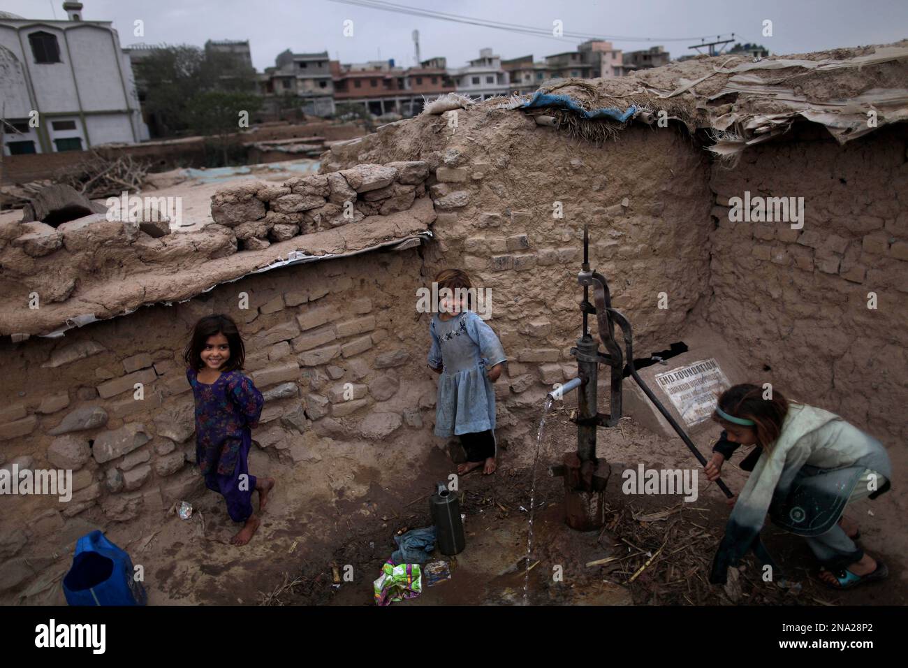 Pakistani girls smile while collecting water from a hand pump in a slum ...