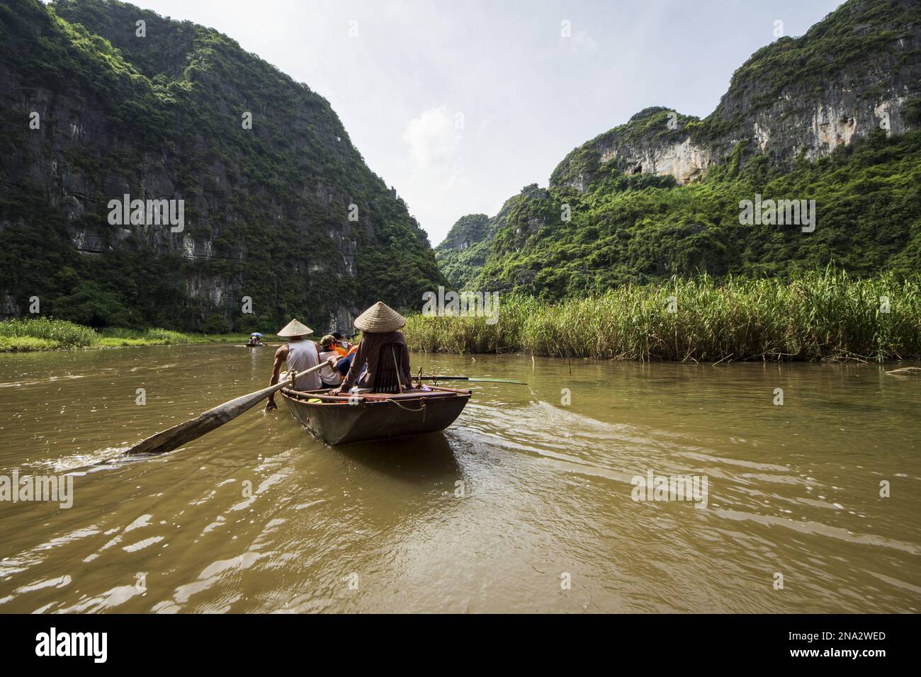 People in a boat on the Ngo Dong River surrounded by limestone karst mountains; Tam Coc, Ninh ...
