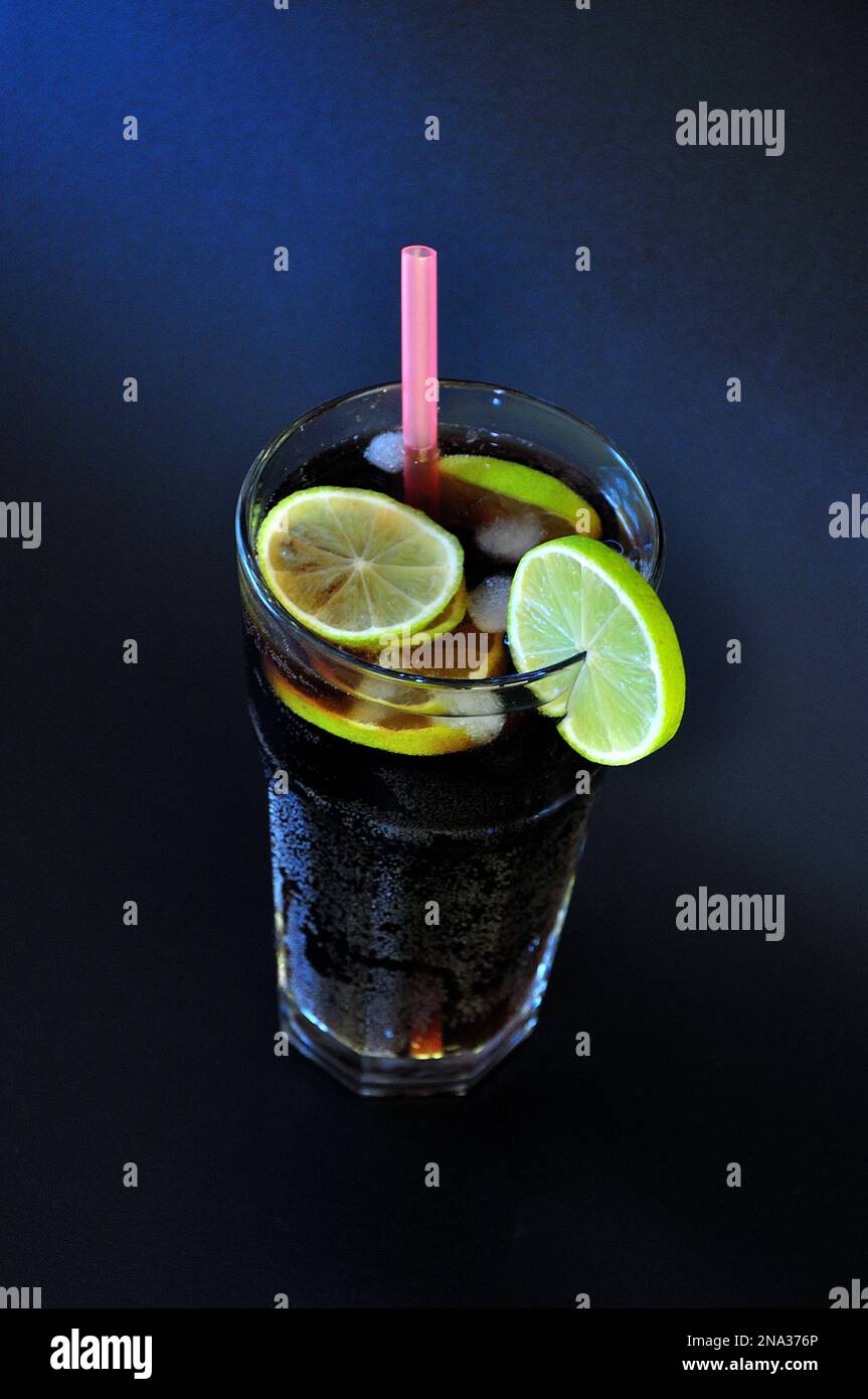 Cola with lime, a refreshing drink in a tall glass with ice and straws ...