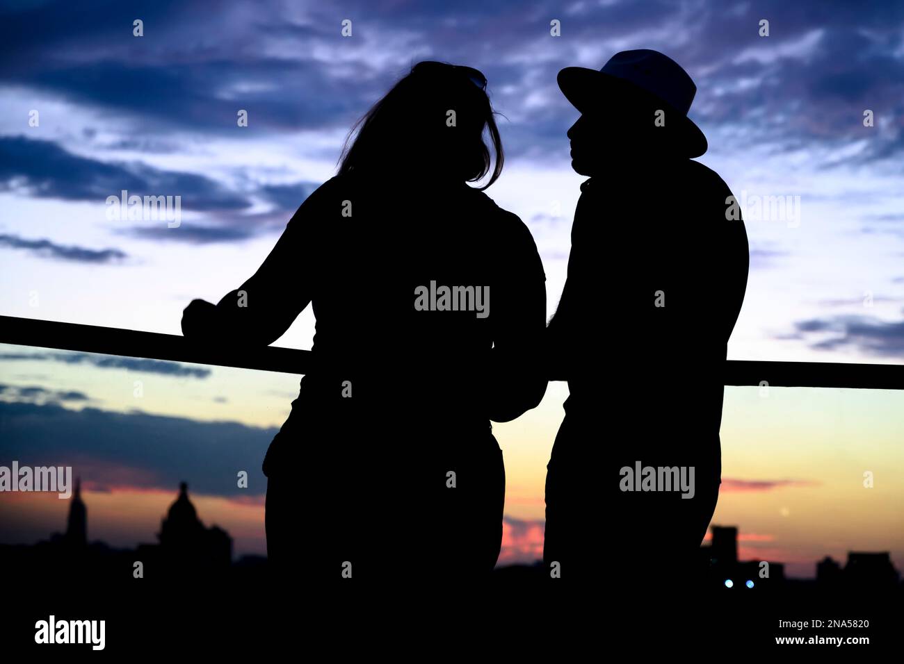 Silhouetted couple stands at a railing overlooking the skyline of ...