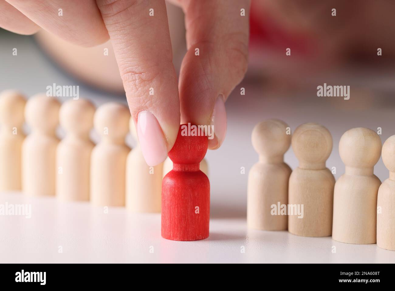 Human hand takes one red figure from group of many ordinary wooden ...