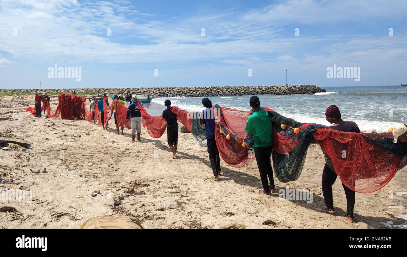 Photo of a group of fishermen walking in a line at the sea shore with a ...