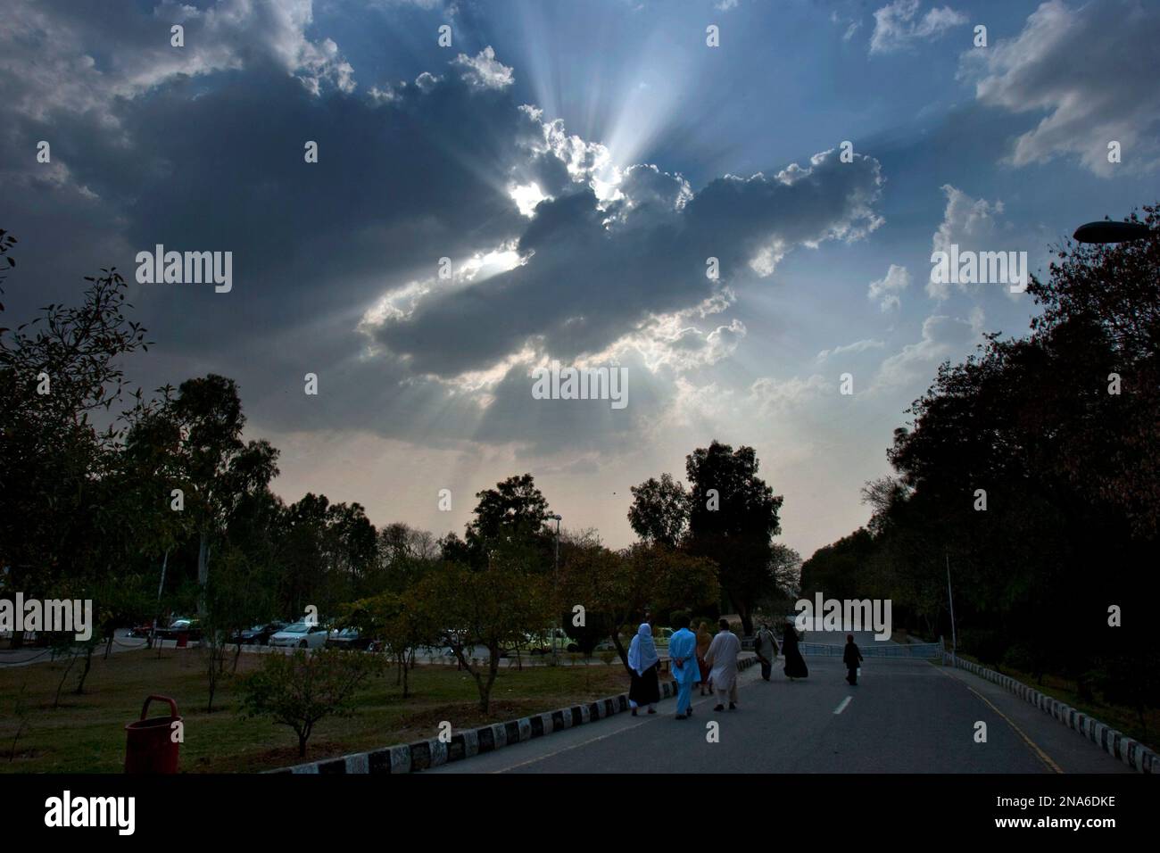 A Pakistani family walk in a park as sun rays shine through clouds in ...