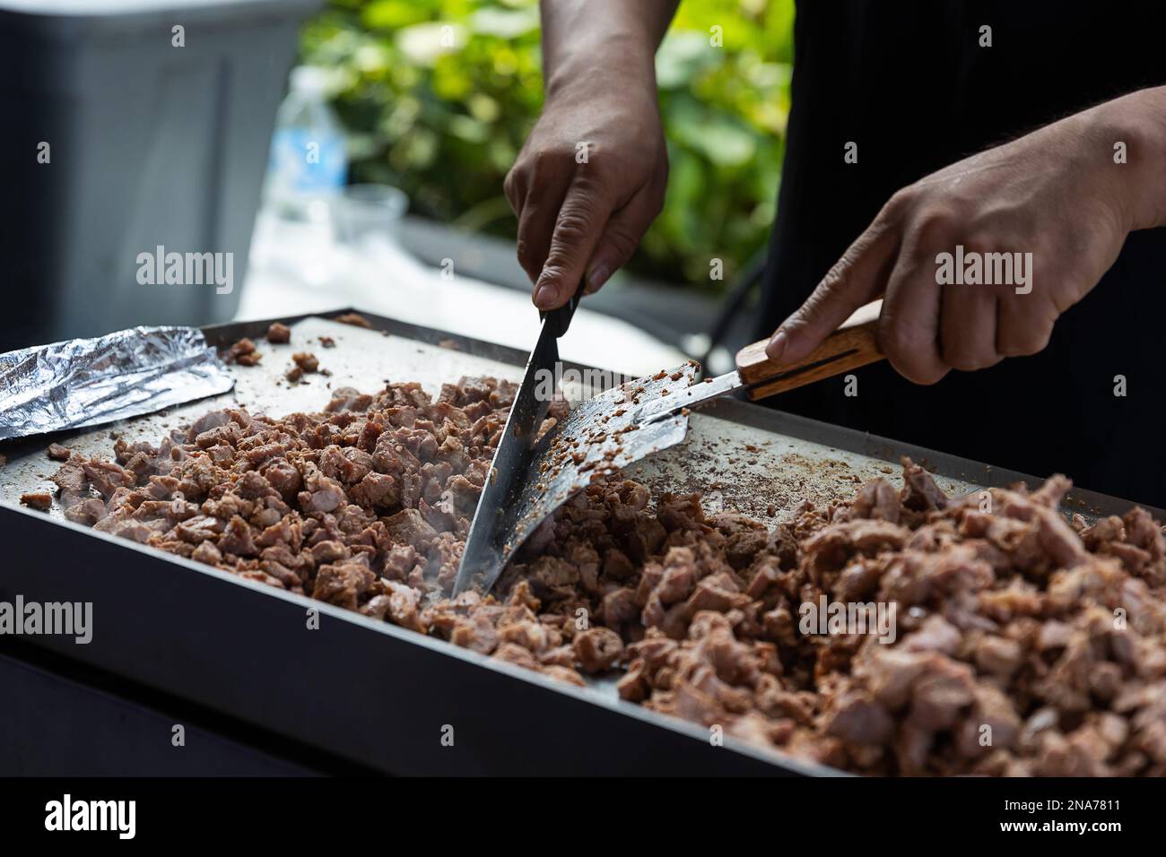 A closeup of a Mexican taquero making the pastor meat in the center of ...