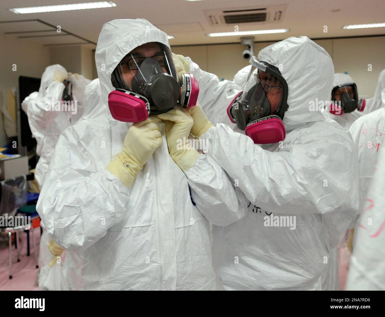 A journalist is assisted by TEPCO worker to wear a full-face mask ...