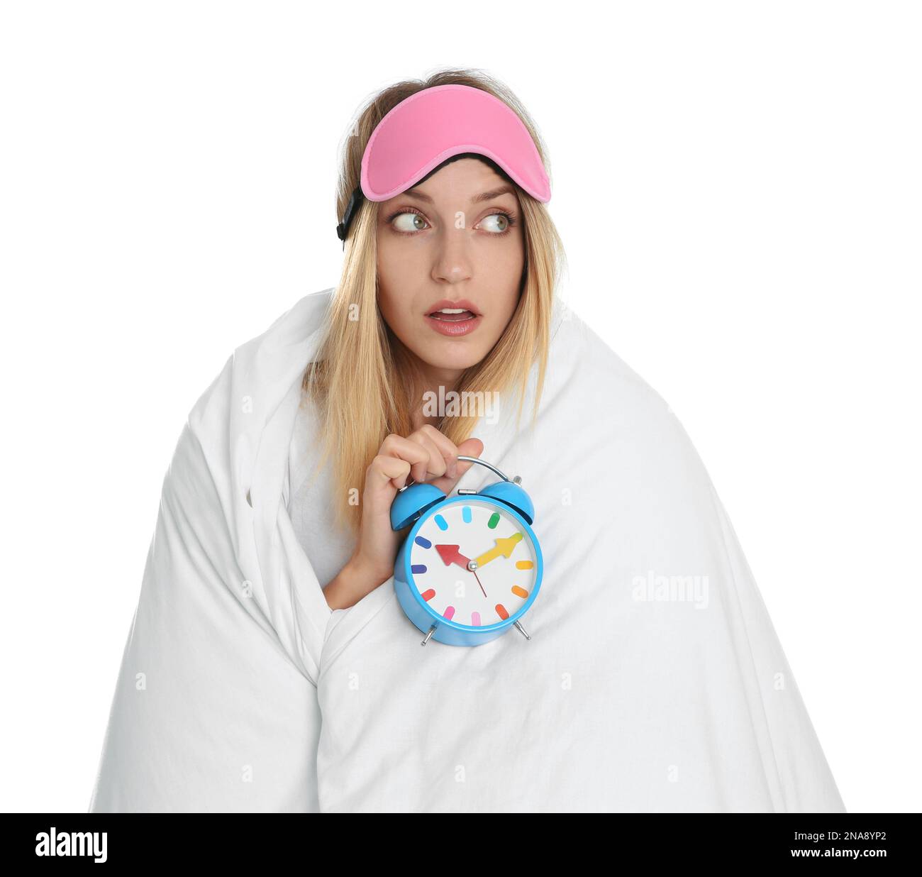 Emotional woman in sleeping mask wrapped with blanket holding alarm ...
