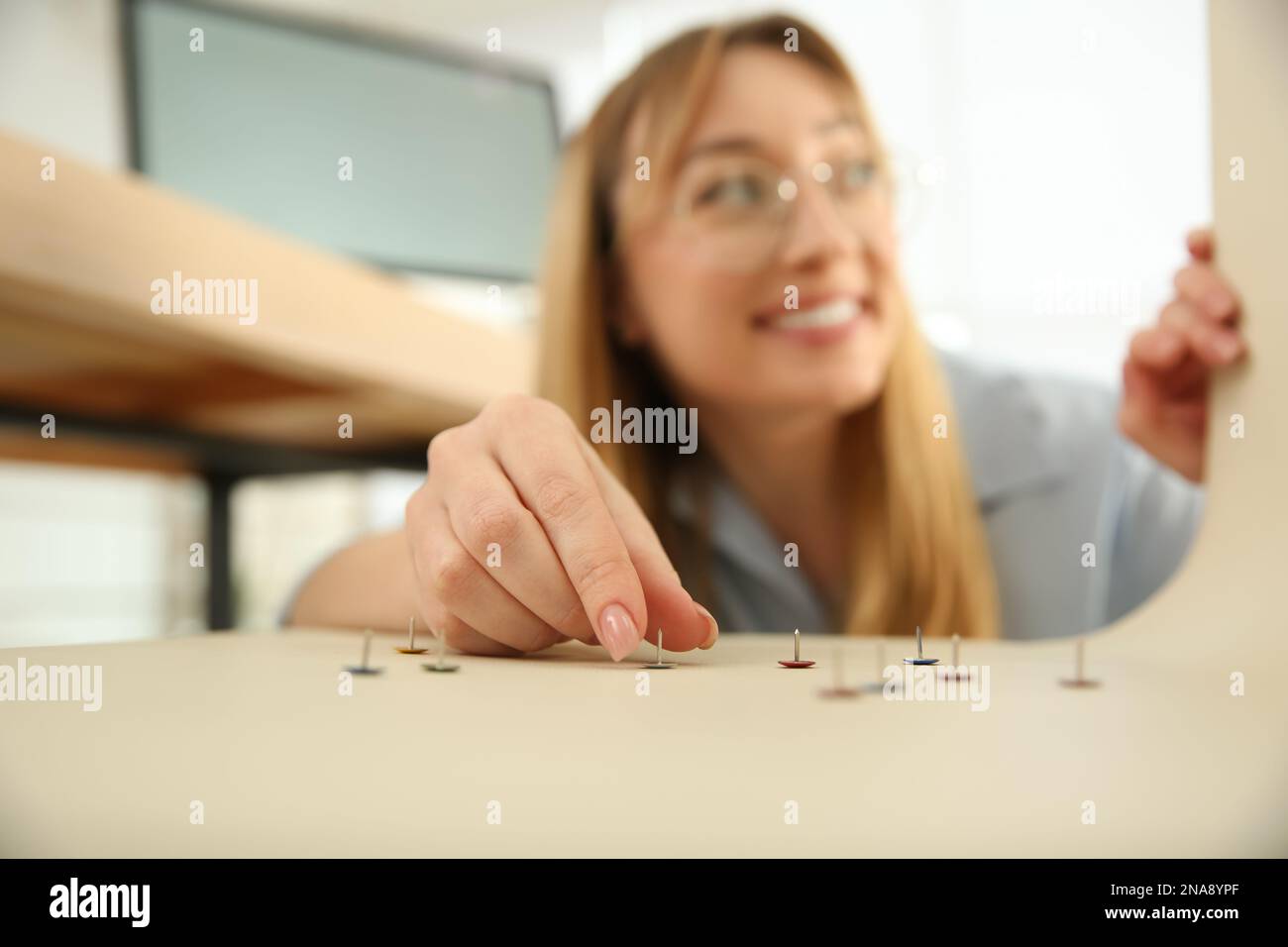 Young woman putting pins on colleague's chair in office. Funny joke ...