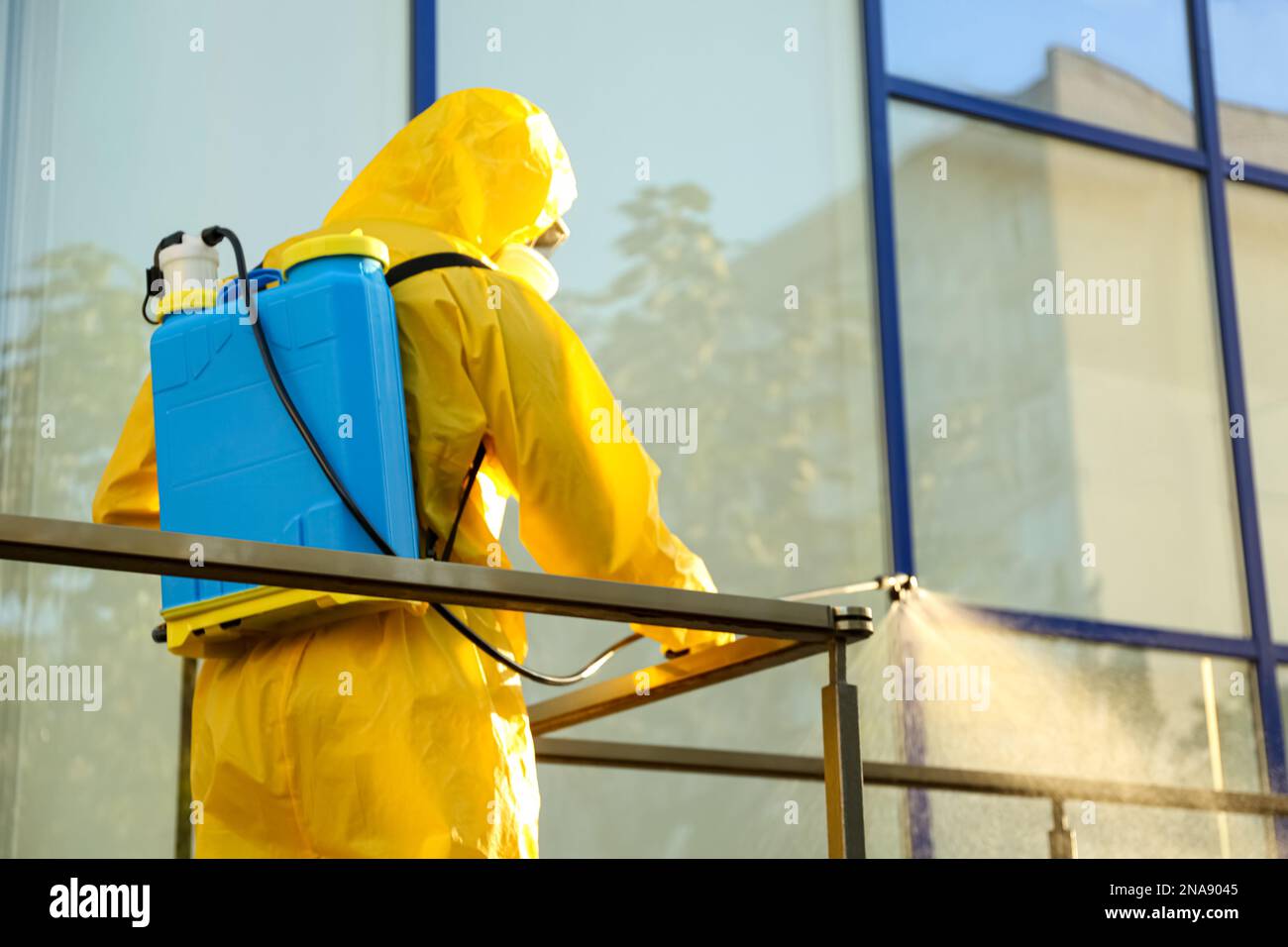 Person in hazmat suit with disinfectant sprayer cleaning metal railing ...