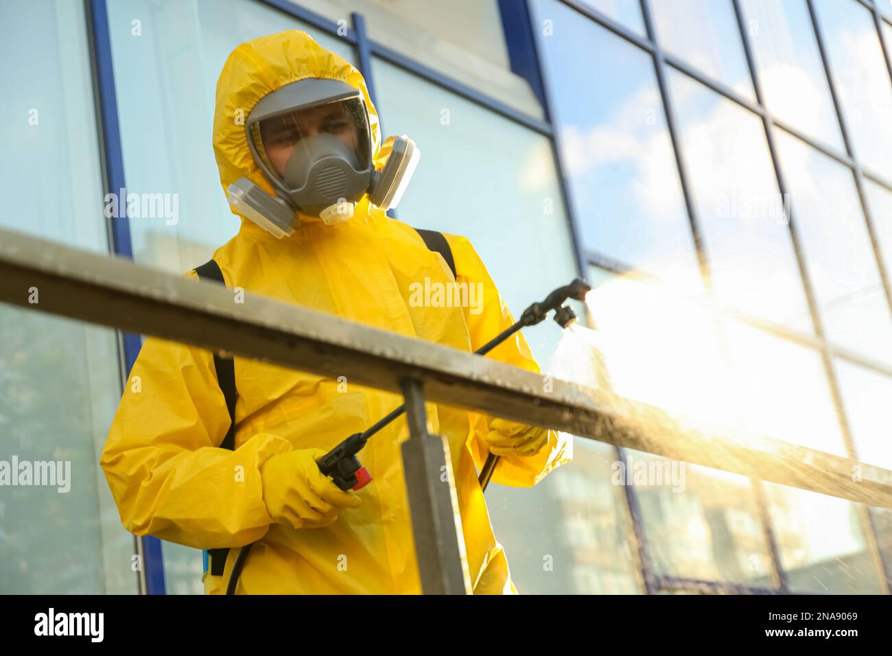 Person in hazmat suit with disinfectant sprayer cleaning metal railing ...