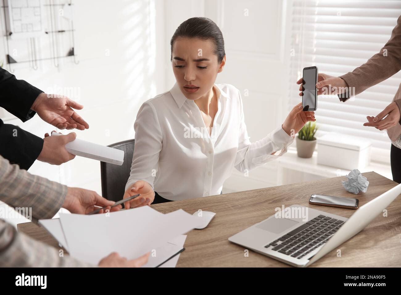 Stressed and tired young woman surrounded by colleagues at workplace ...