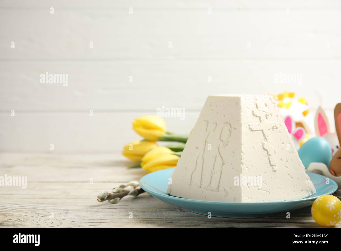 Traditional cottage cheese Easter paskha and dyed eggs on white wooden table, space for text ...