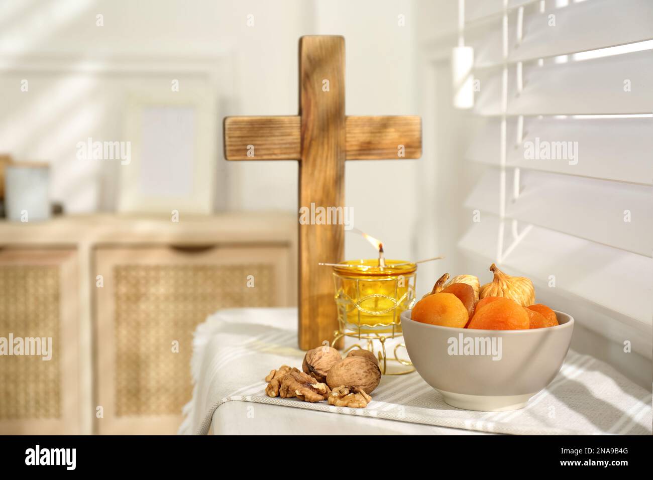 Dried fruits, walnuts, candle and wooden cross on window sill indoors ...