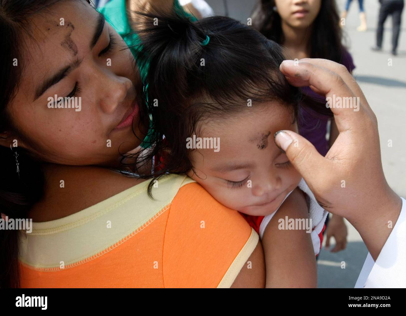A Catholic priest marks the foreheads of devotees with black ashes in ...