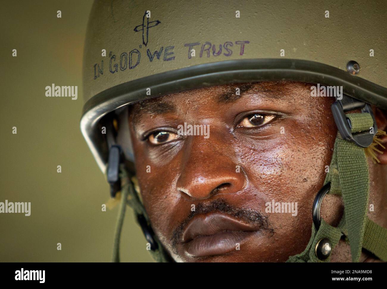 A Kenyan army soldier wears a helmet on which he has written "In God we ...