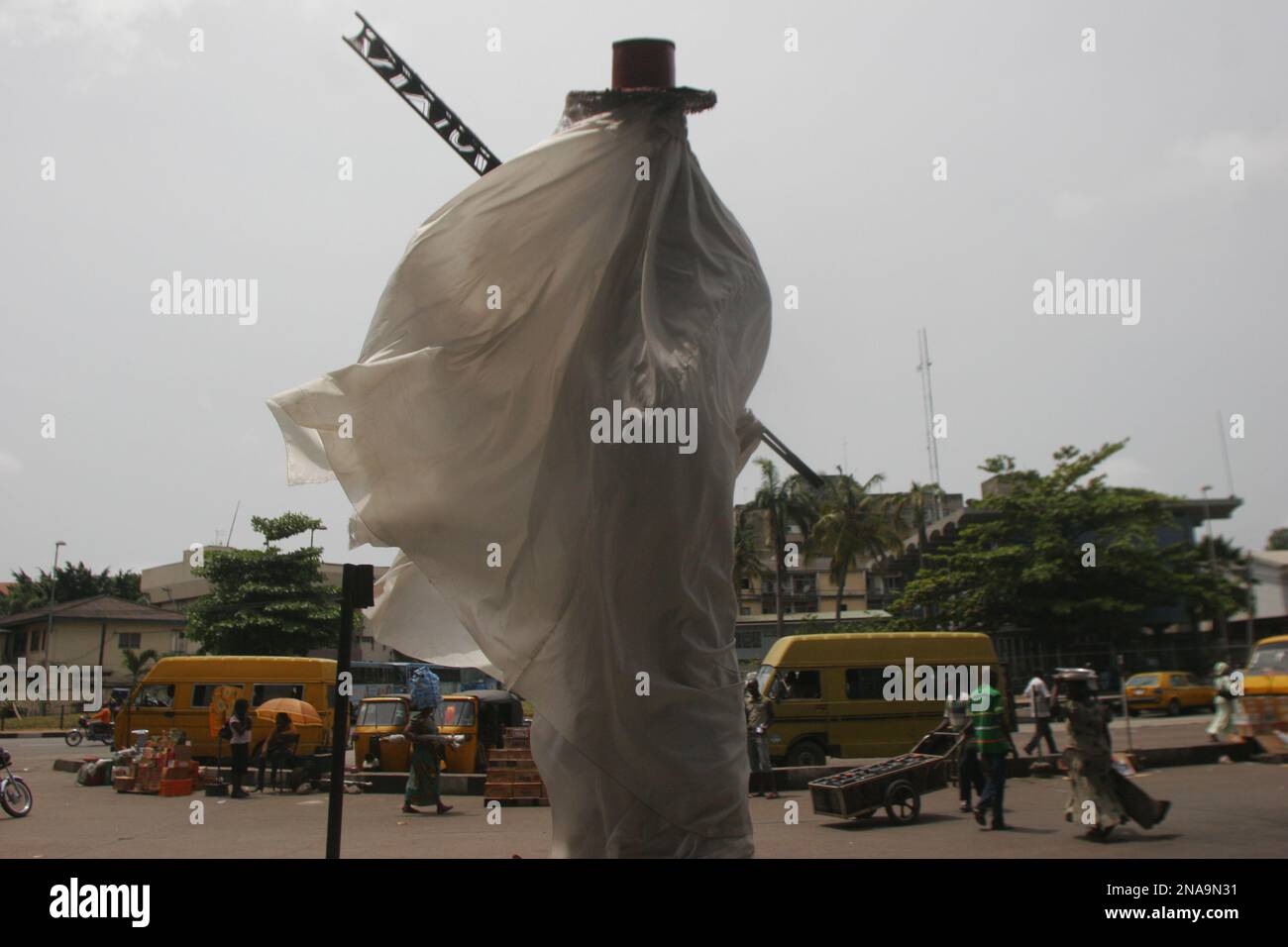 Commuters walk past a statue of an Eyo masquerade at Tafawa Balewa ...