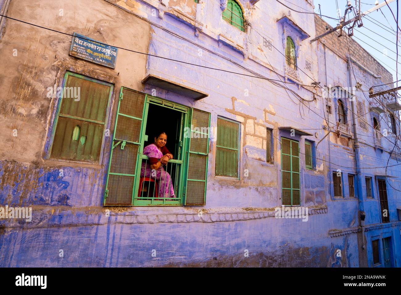 Woman looking out of a window in neighbourhood street of Jodhpur, Blue ...