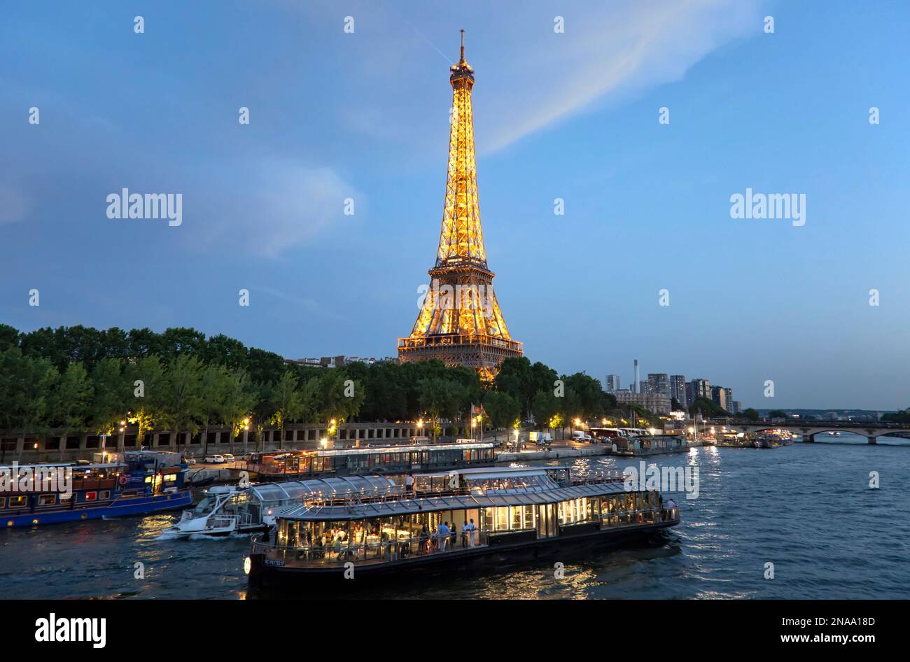 Eiffel Tower illuminated at dusk and riverboats sailing the Seine in ...