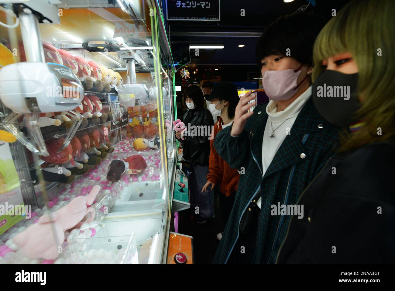 Japanese teenagers trying to pick toys in a toy crane claw machine in ...