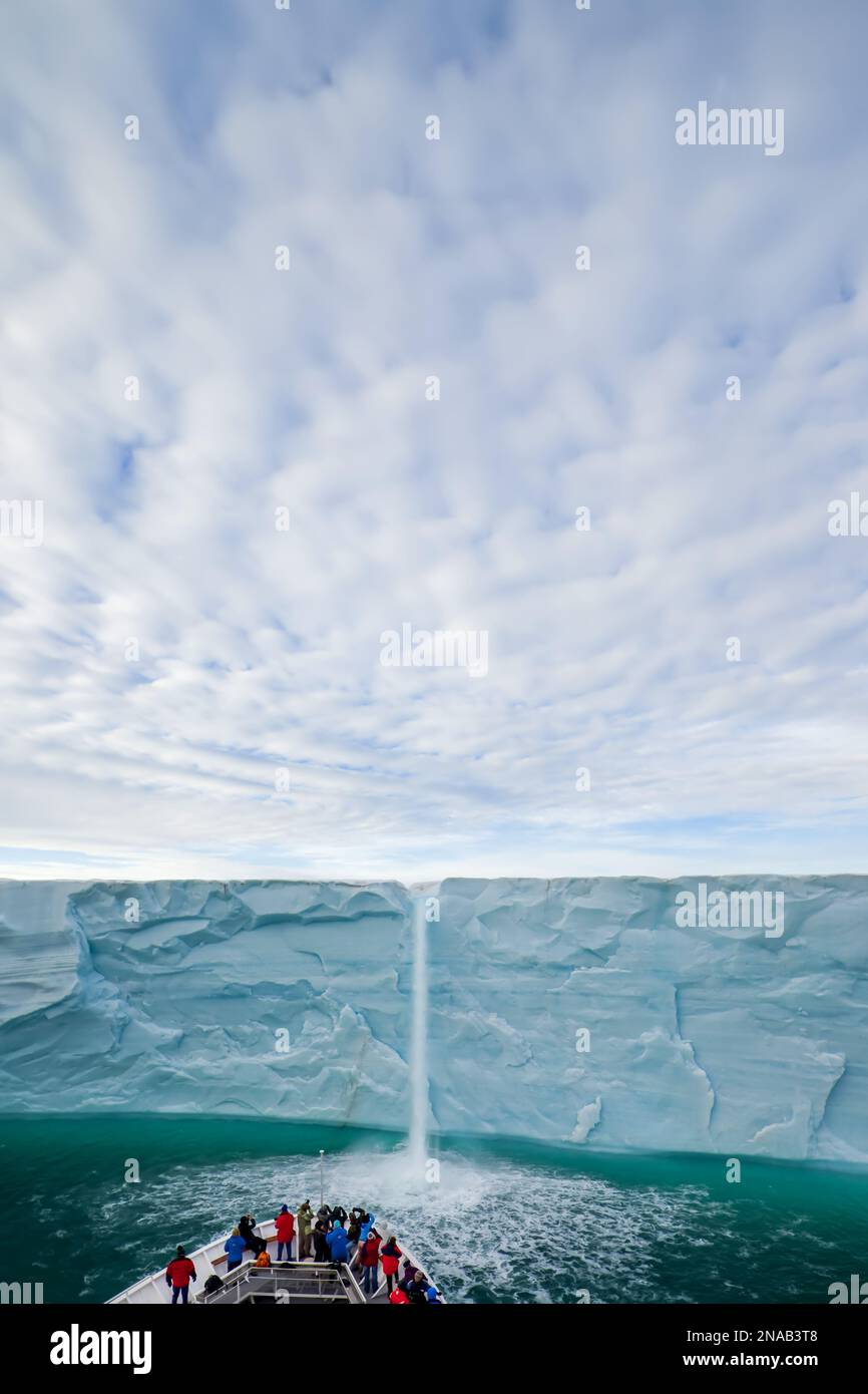 Tourists watch a meltwater waterfall on an icecap from a cruise ship ...
