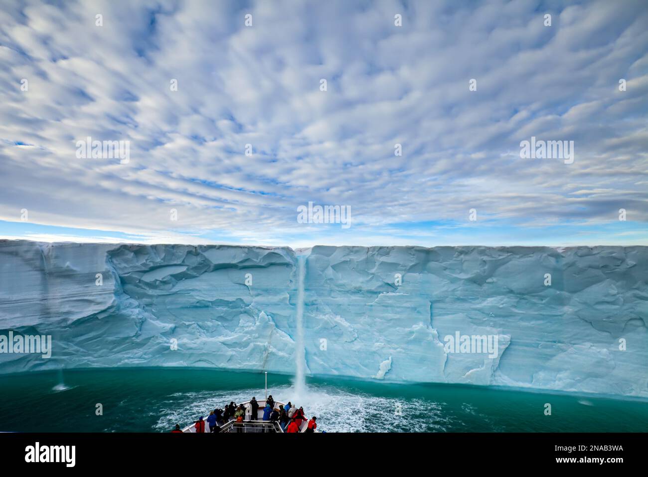 Tourists watch a meltwater waterfall on an icecap from a cruise ship ...