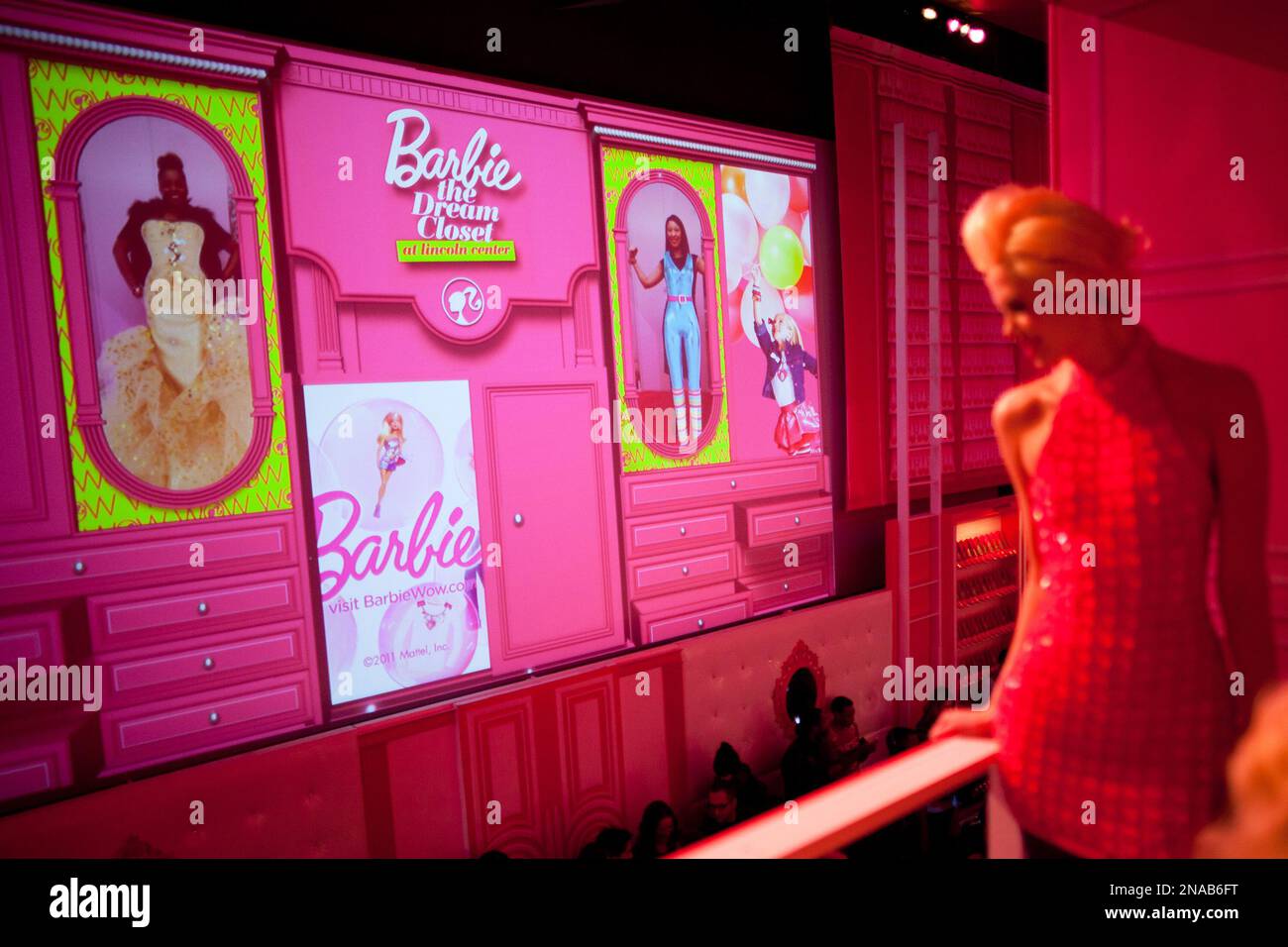 A model dressed as a Barbie Doll looks out onto the crowd as images of ...