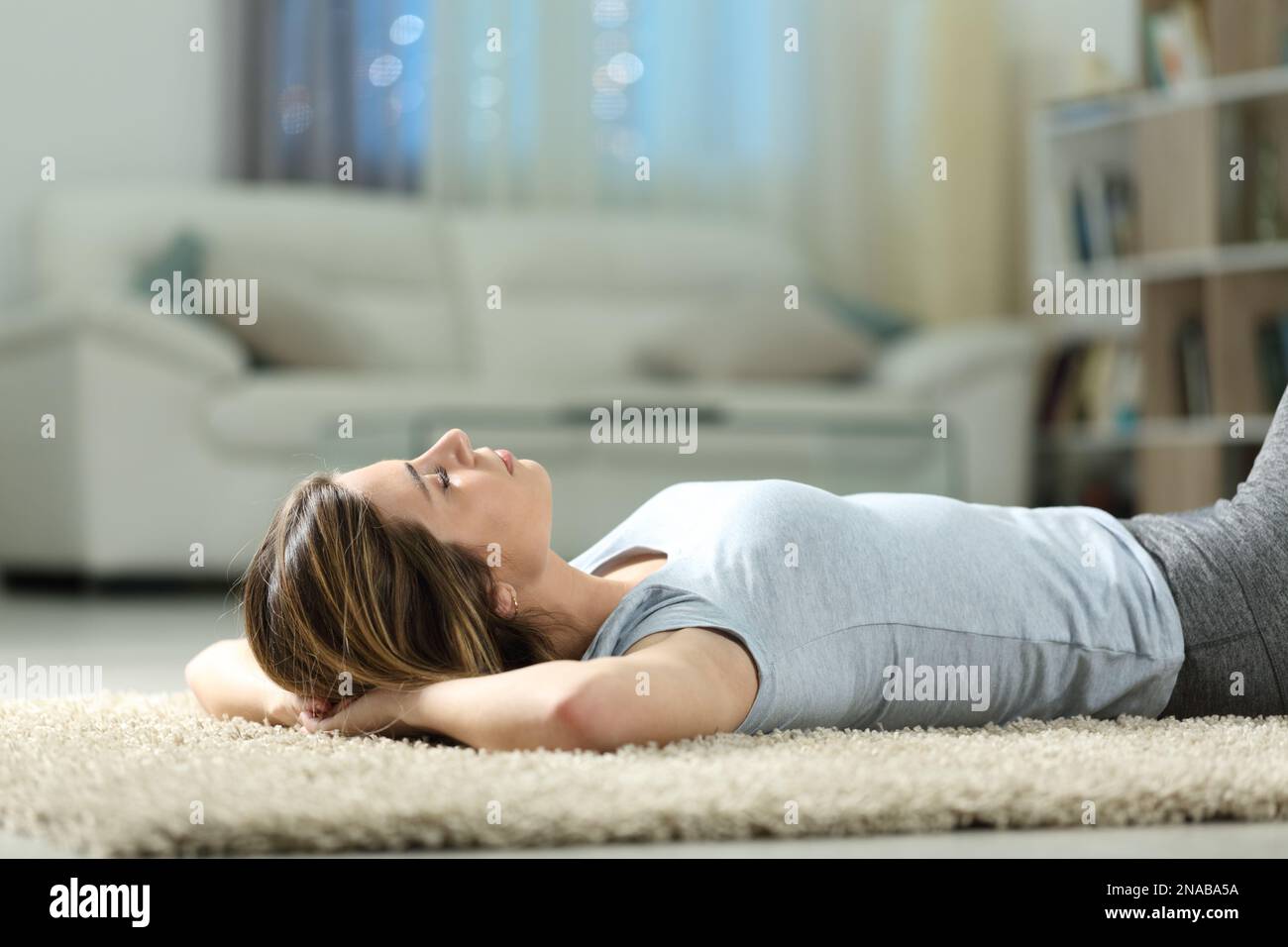 Woman resting lying on a carpet in the night at home with arms on head ...