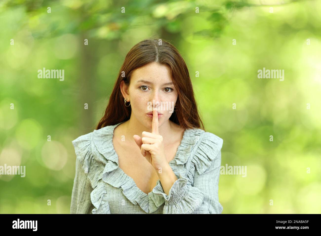 Front view portrait of a woman who is asking for silence in a forest ...
