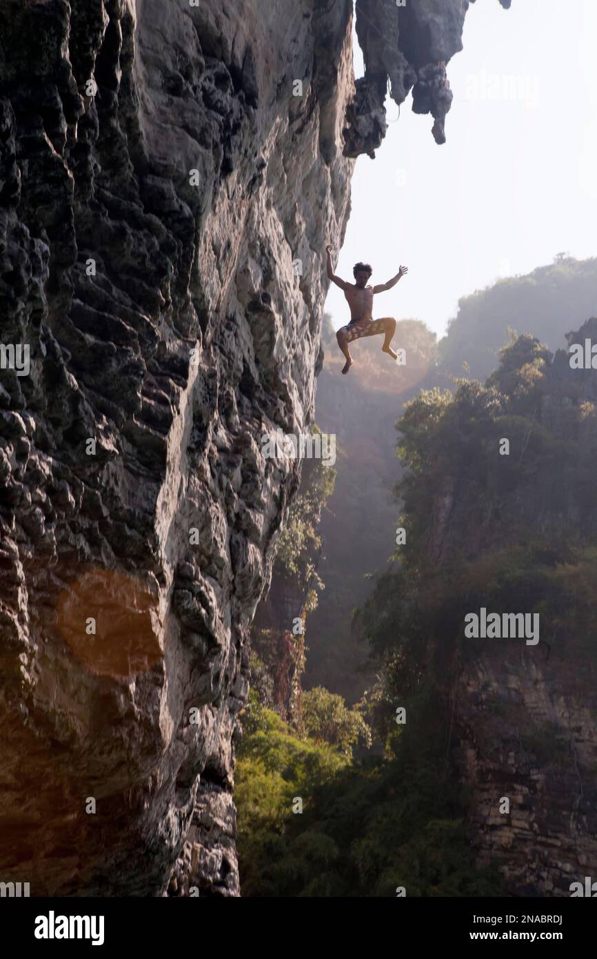 A climber deep water soloing on the limestone cliffs of a karst drops ...